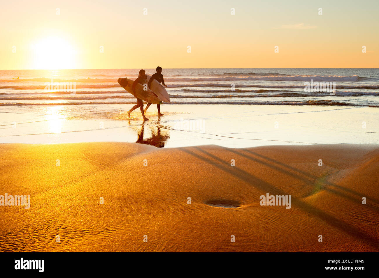 Two surfer running on the beach at sunset. Portugal has one of the best ...