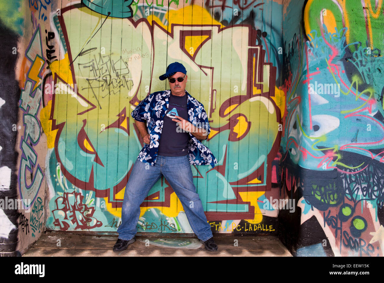 Mature male makes a gangster pose in front of a graffiti background ...