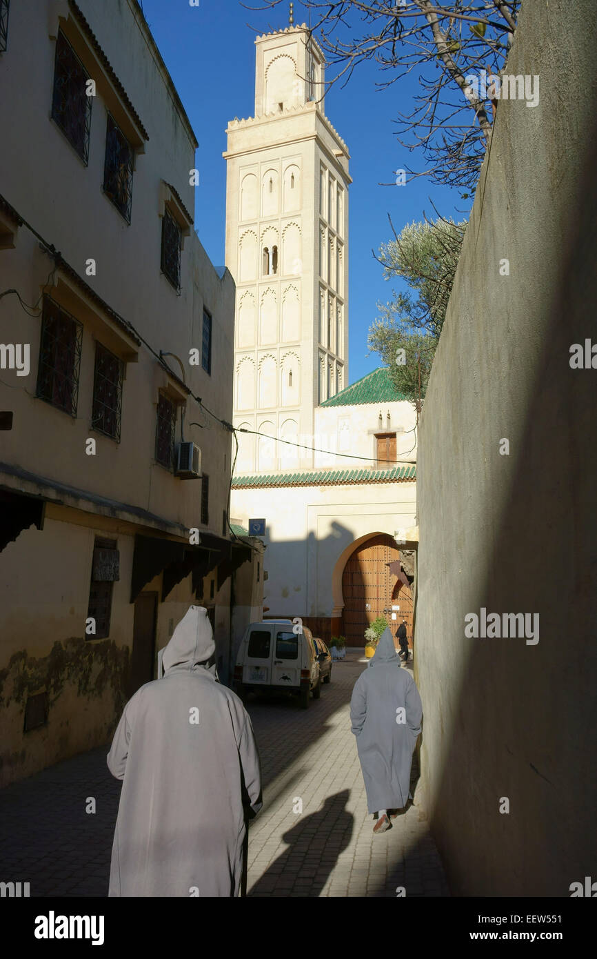 Moroccan men walking wearing traditional hooded djellaba, minaret of ...
