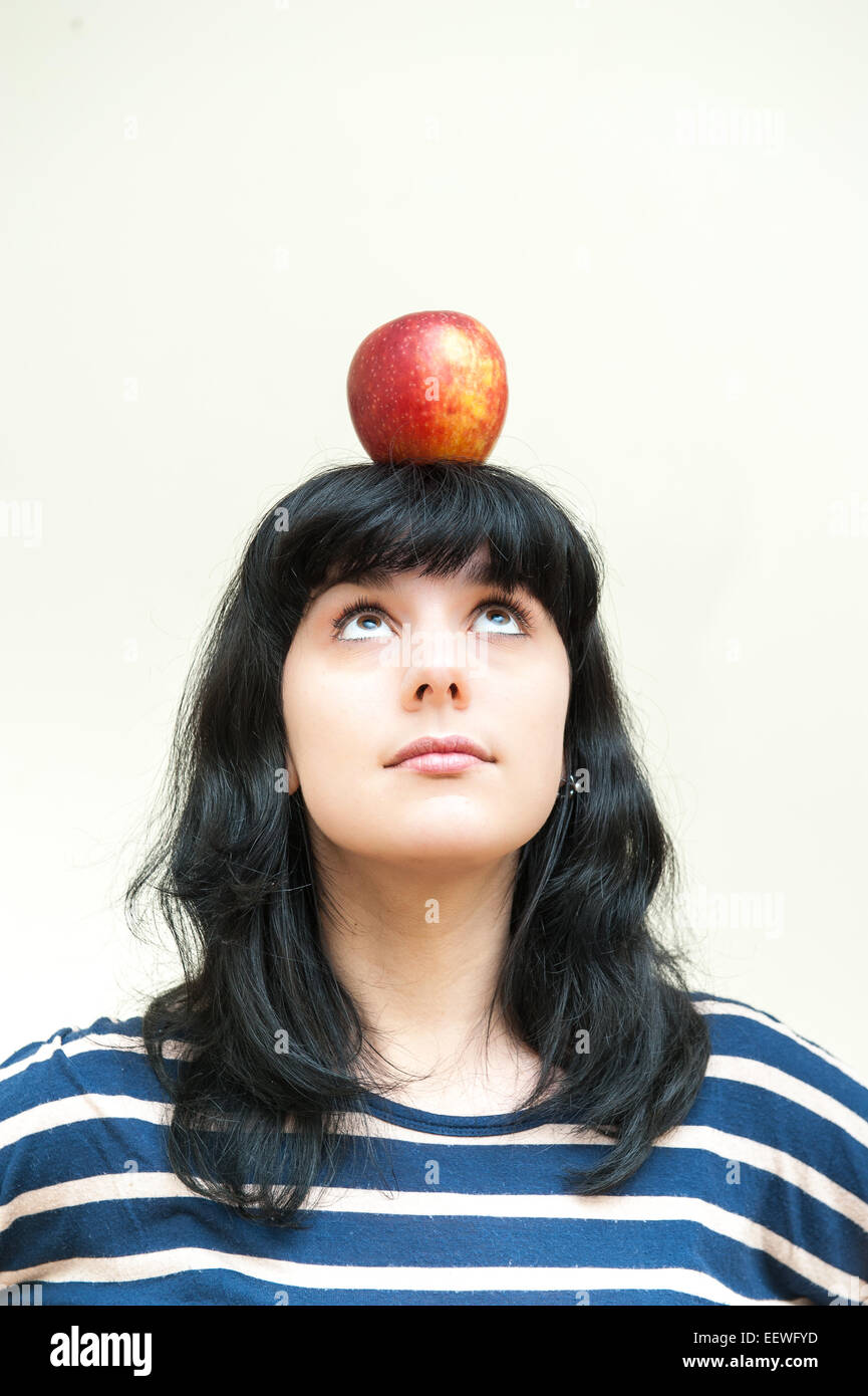 Pretty brunette girl looking red apple on her head on white background ...