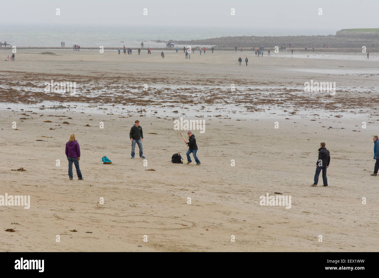 Family of holiday-makers playing cricket on cold wet autumn day on the ...