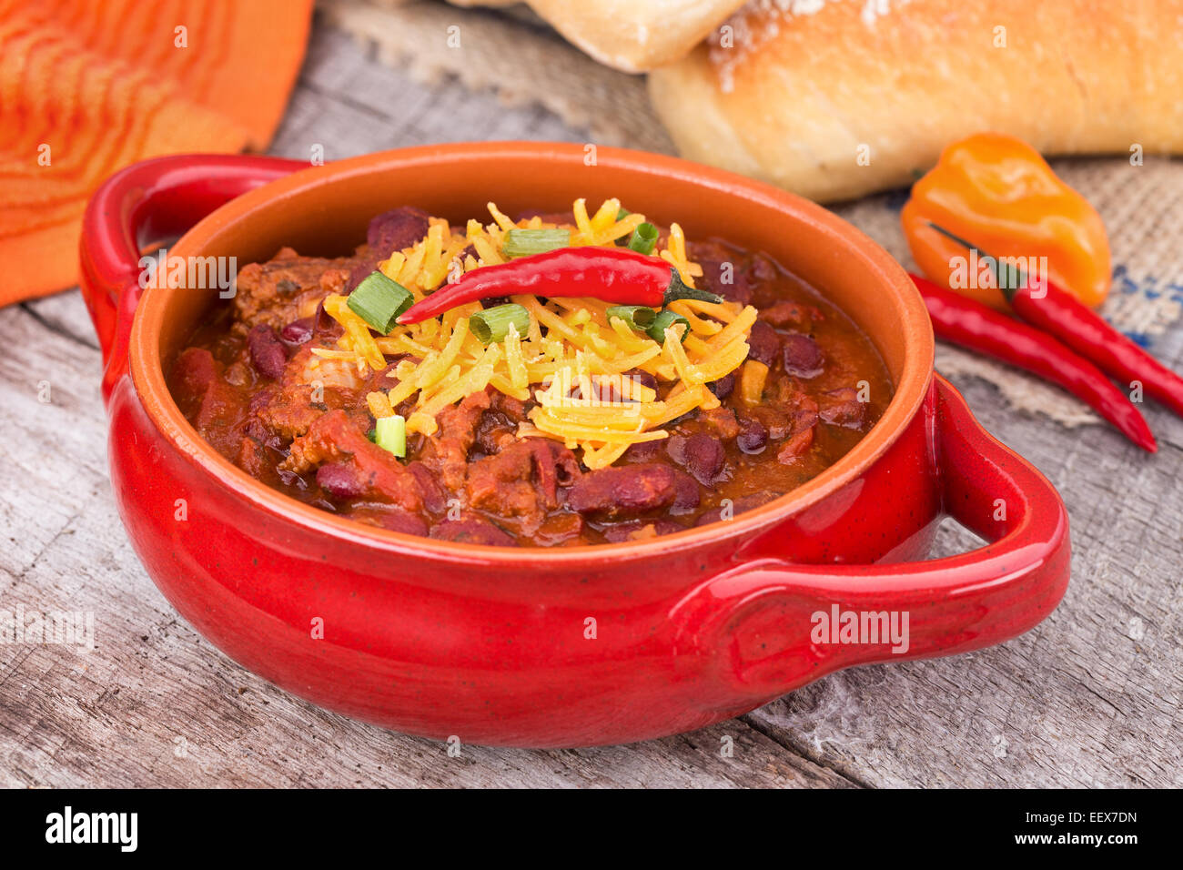 Ceramic crock of meat and bean chili garnished with shredded cheddar ...
