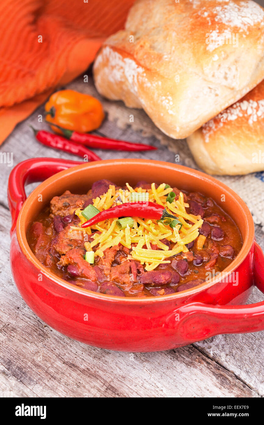 Ceramic crock of meat and bean chili garnished with shredded cheddar ...