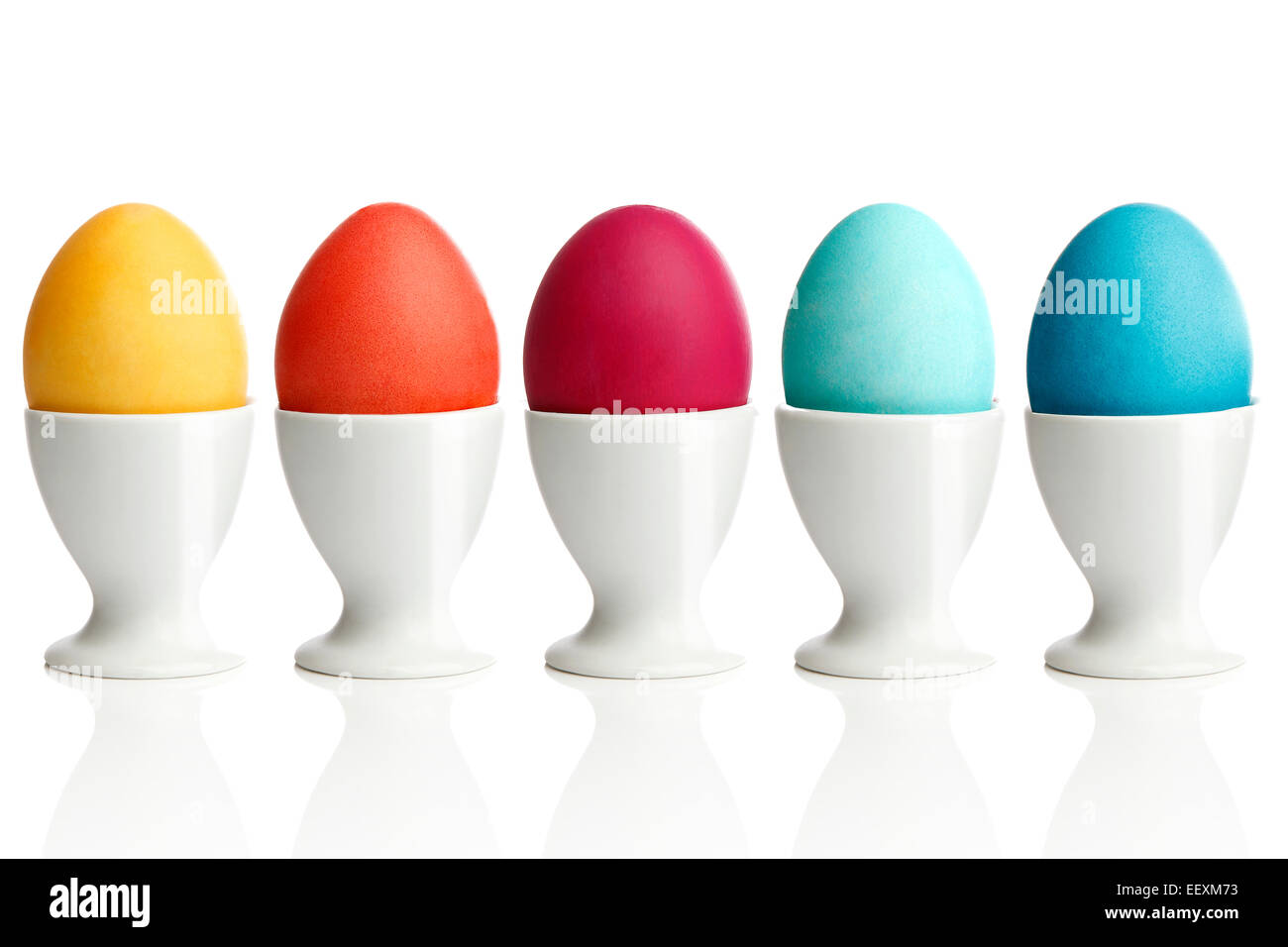 Colored Easter eggs in white egg cups in front of a white background ...