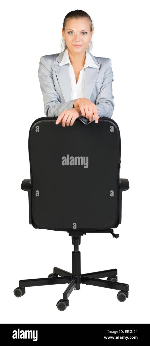 Businesswoman kneeling on office chair, looking at camera cheerfully ...