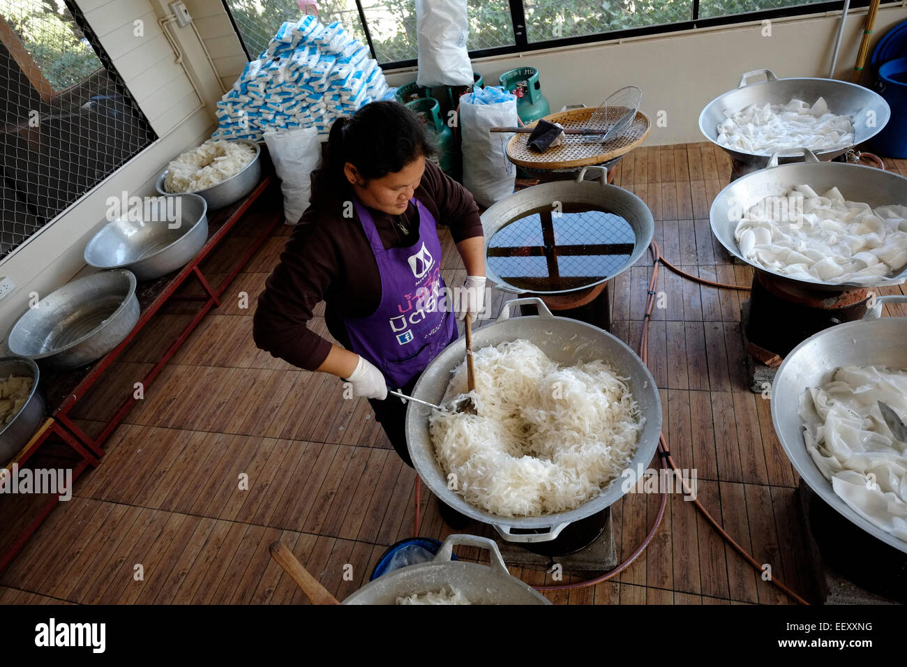 A Thai woman cooking thin slices of coconut in boiling water and sugar ...