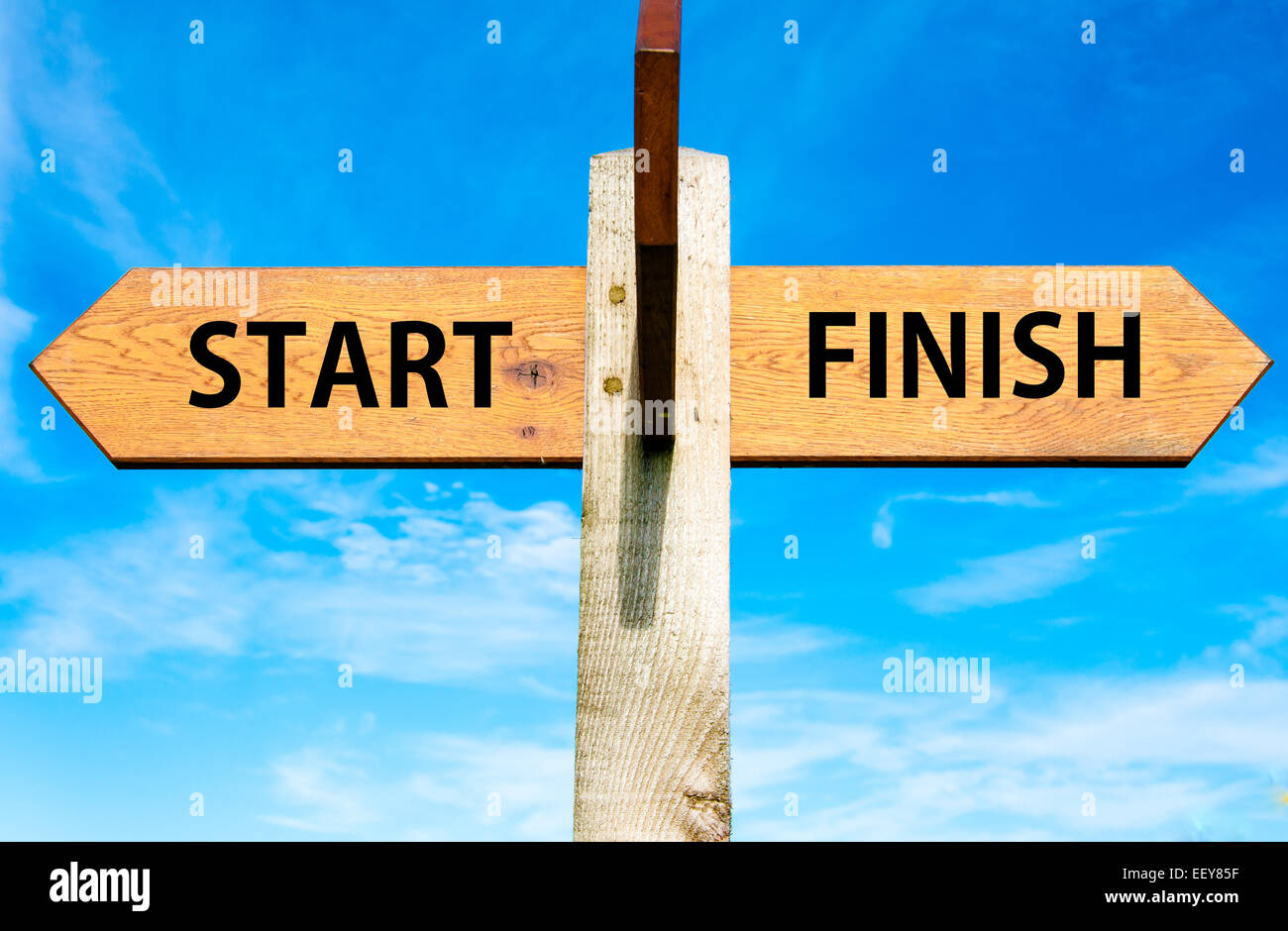 Wooden signpost with two opposite arrows over clear blue sky, Start ...