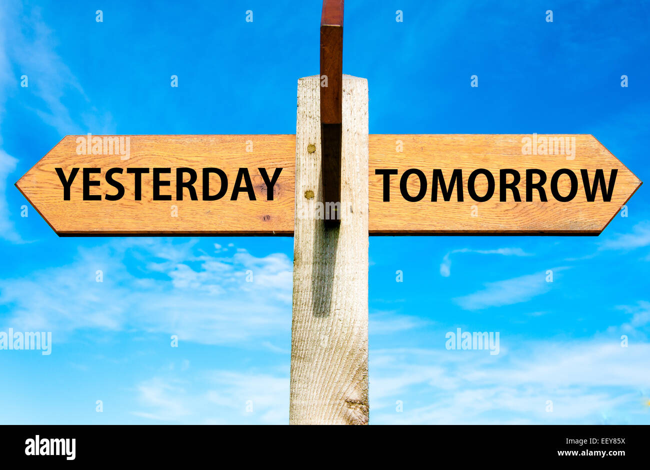 Wooden signpost with two opposite arrows over clear blue sky, Yesterday ...
