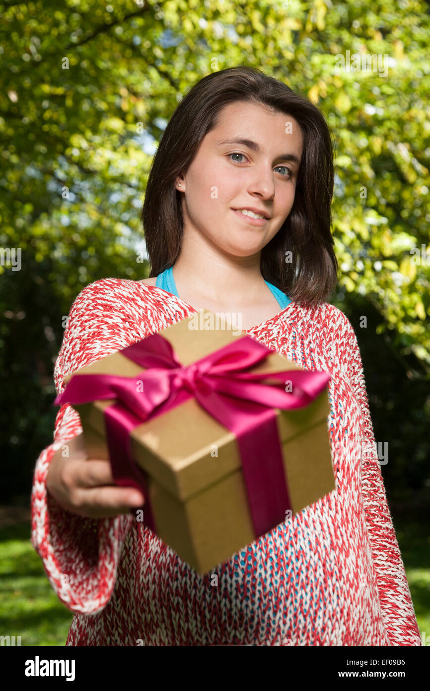 young woman offering golden red gift box over green tree background ...
