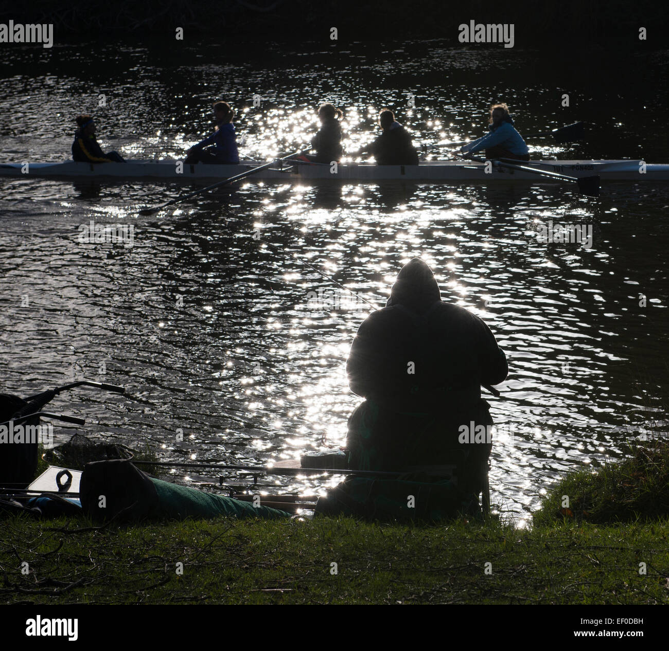 A rowing team passes a fisherman silhouetted by winter sunshine on the ...