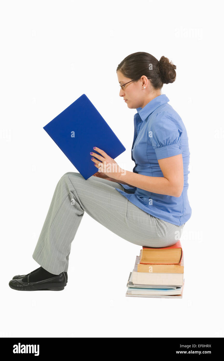 Woman reading while sitting on a stack of books Stock Photo - Alamy