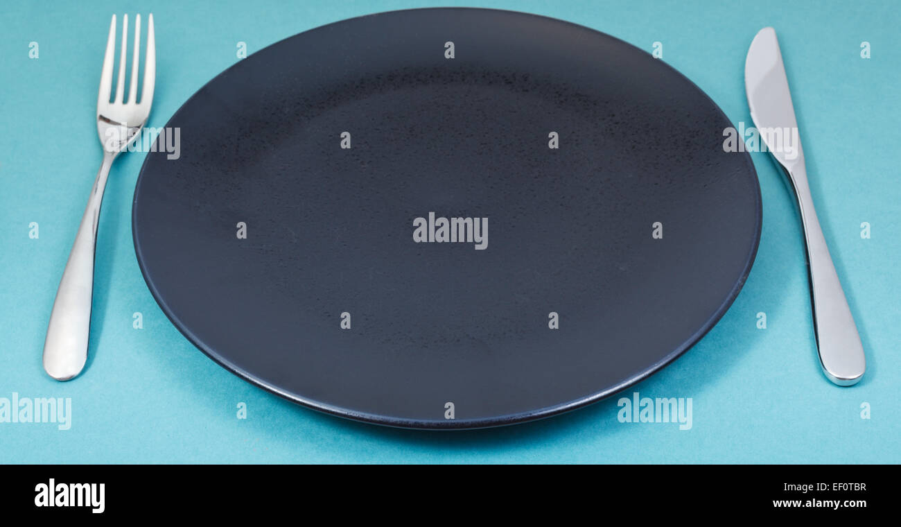 empty dinner black plate with fork and knife set on green background ...