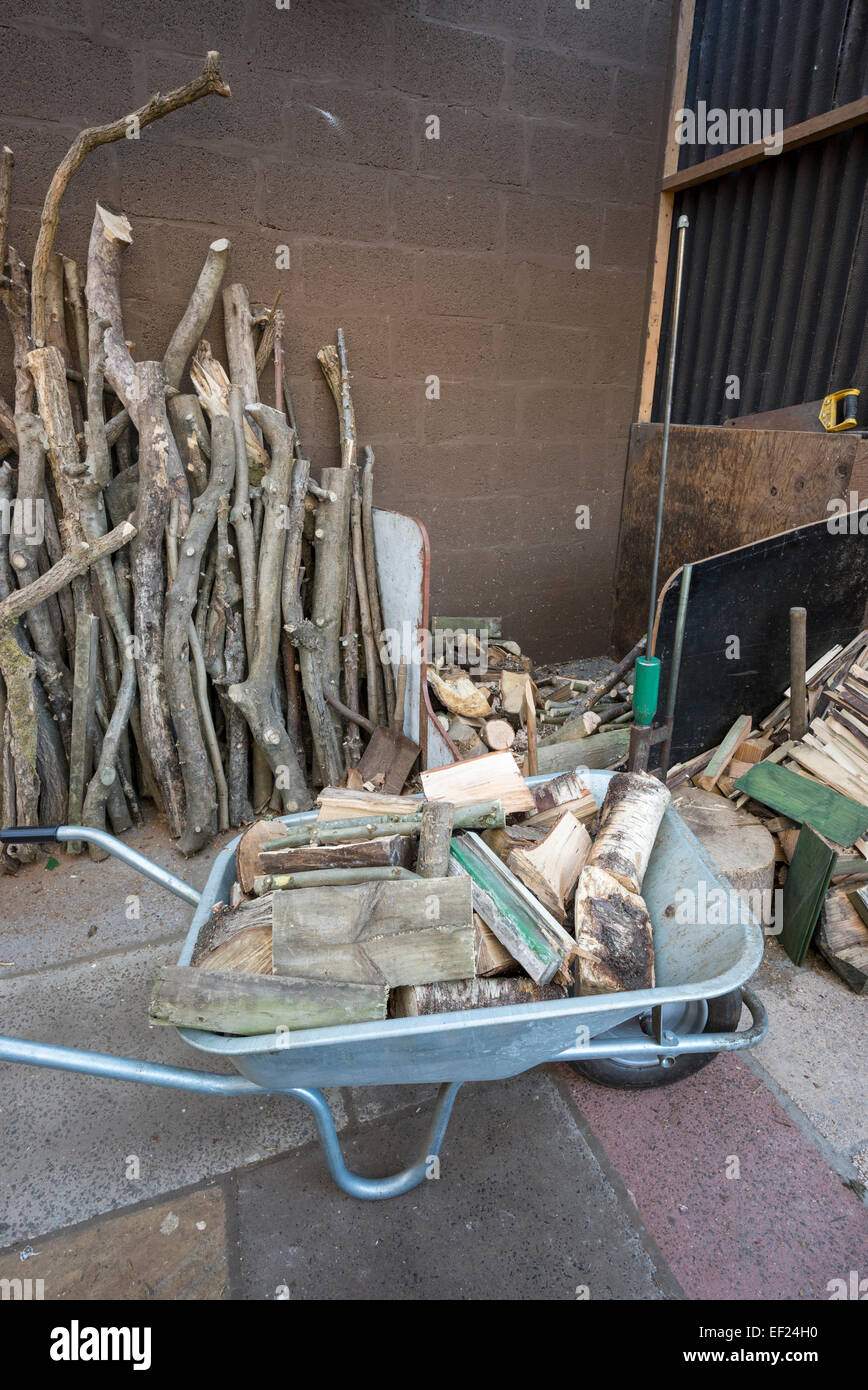 Wheelbarrow full of logs beside a pile of kindling and a log splitter ...