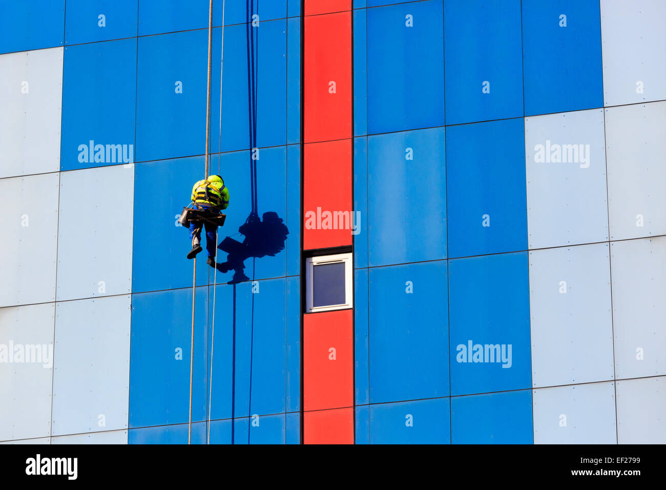 Workman suspended by a rope harness repairing damage to the exterior ...