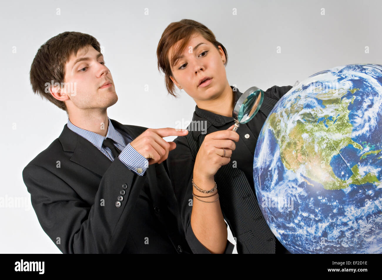 Two people looking at a globe with a magnifying glass Stock Photo - Alamy