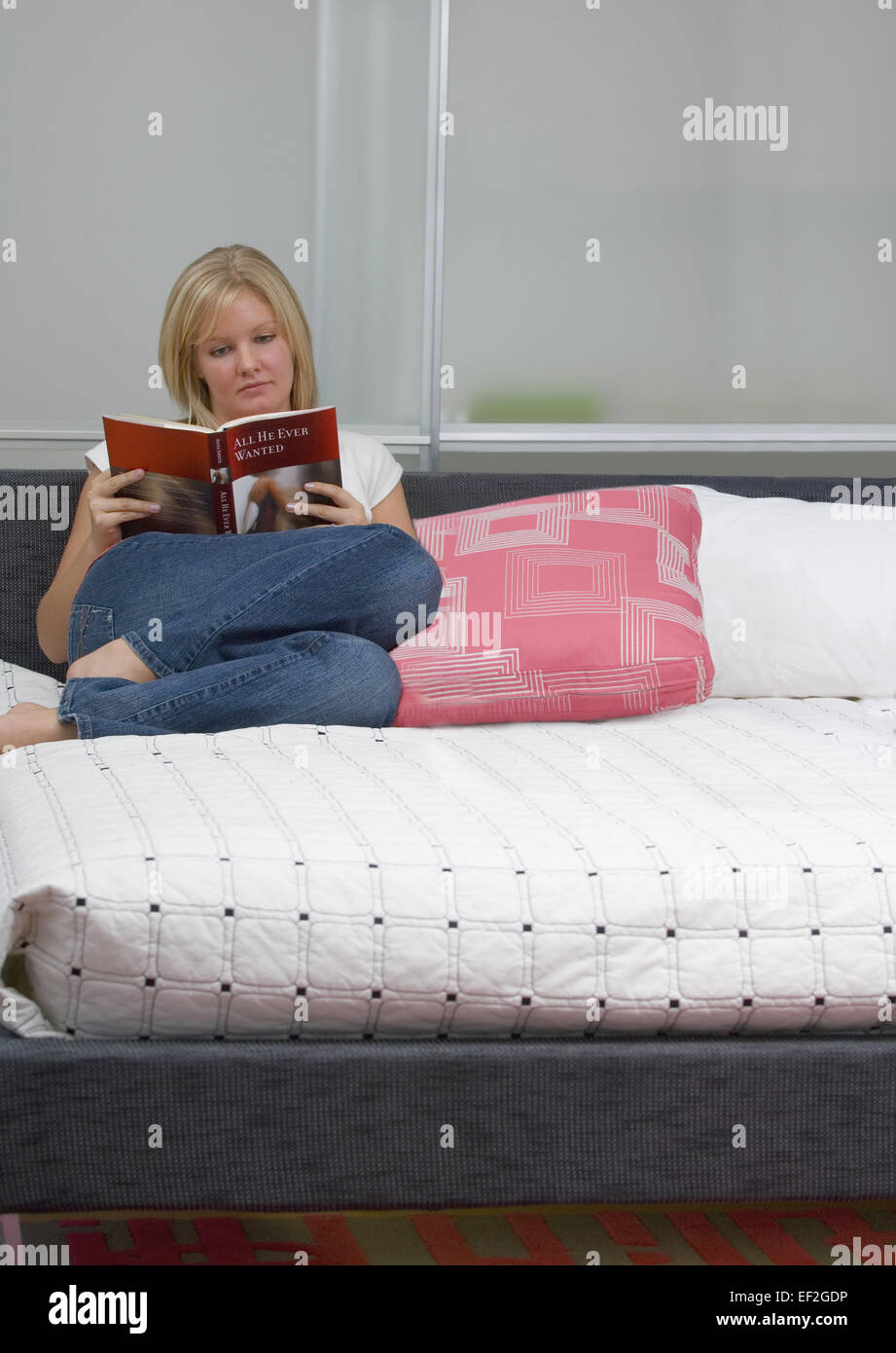 Woman relaxing and reclining on a bed while reading a book Stock Photo ...