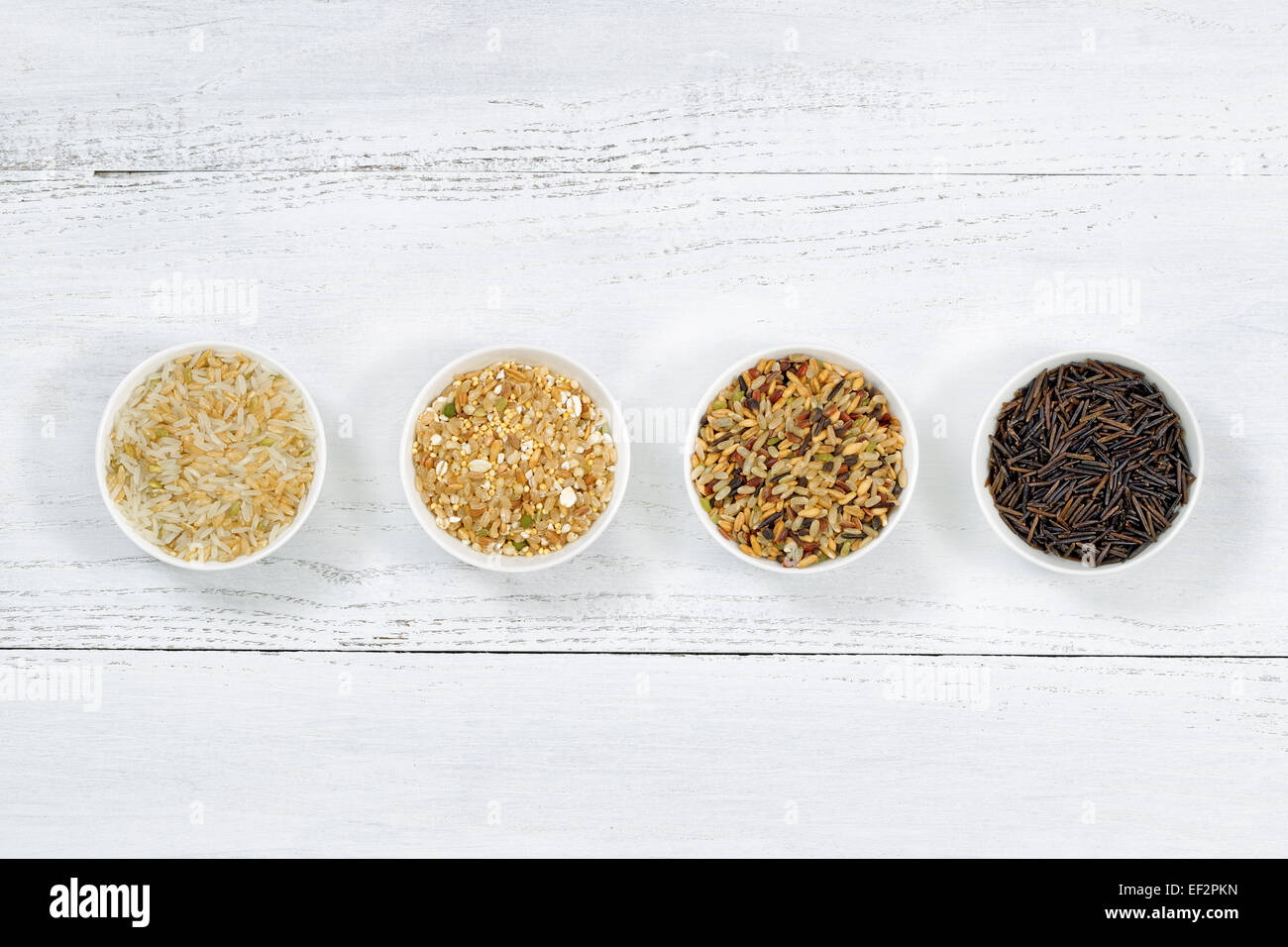 Top view of various rice types each within a small bowl on white wood ...