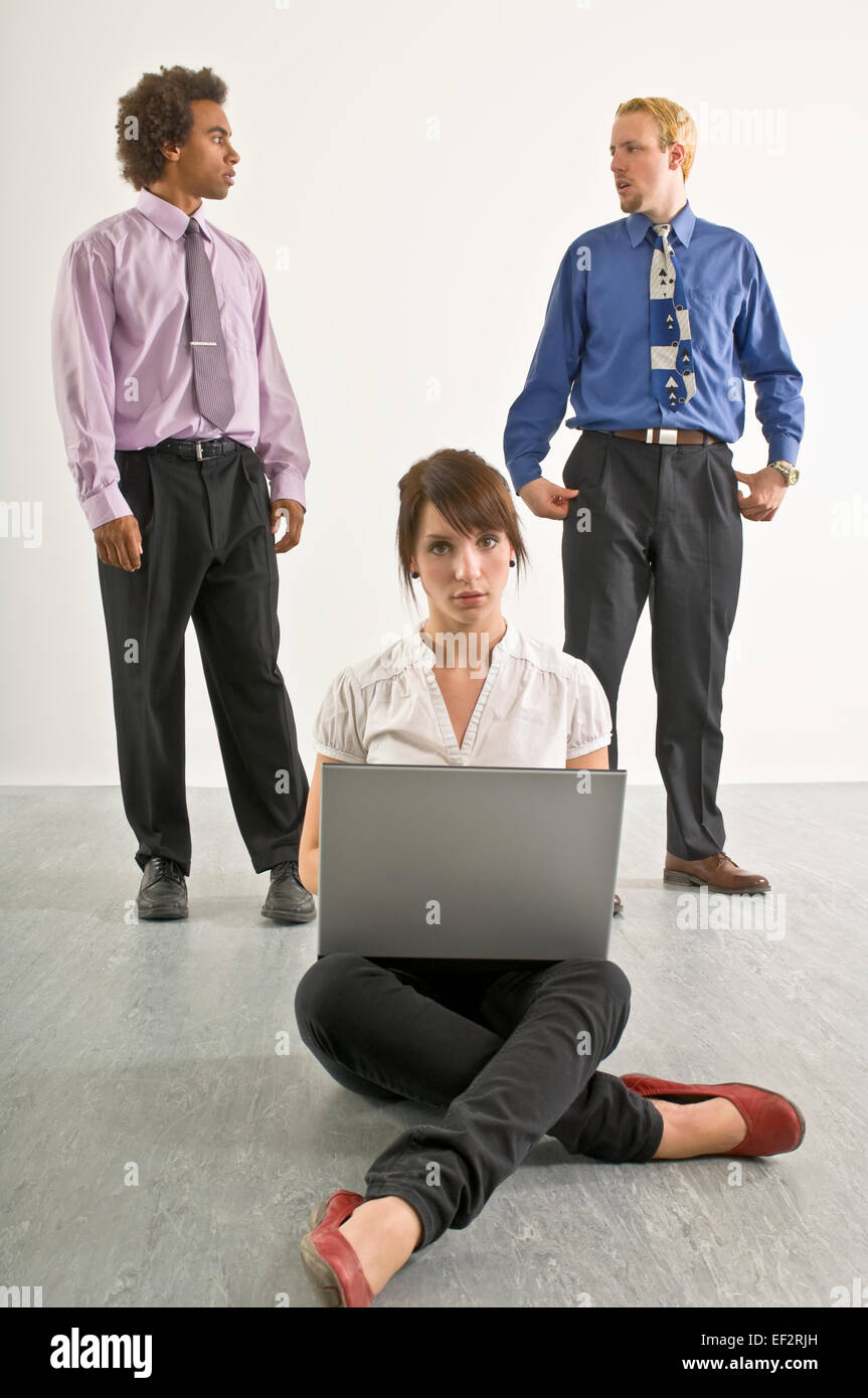 Two businessmen standing behind woman sitting on floor with laptop ...