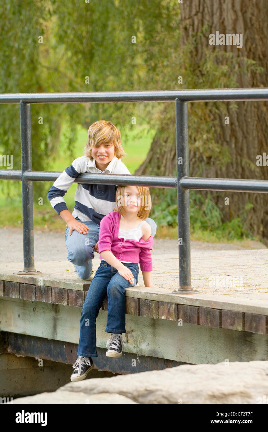 Siblings sitting on bridge Stock Photo - Alamy
