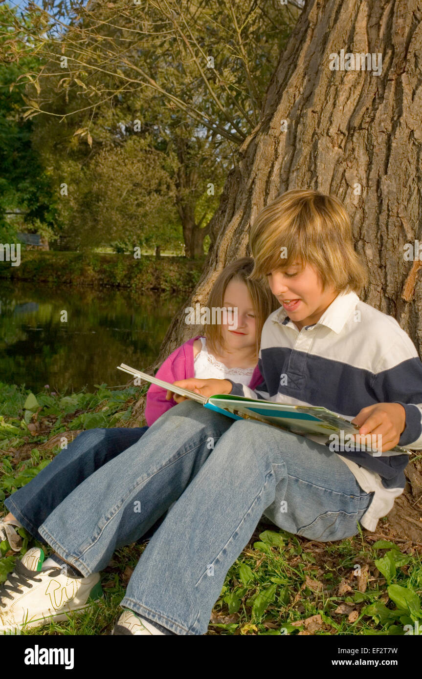 Brother reading book to little sister in park Stock Photo - Alamy