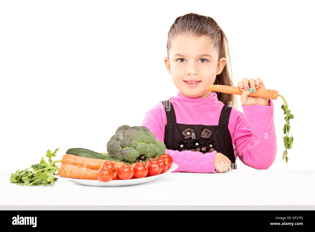 Girl eating a bunch of vegetables seated on table isolated on white ...