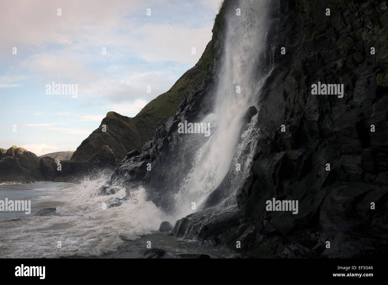 A waterfall cascading over rocks on to the beach in the village of ...