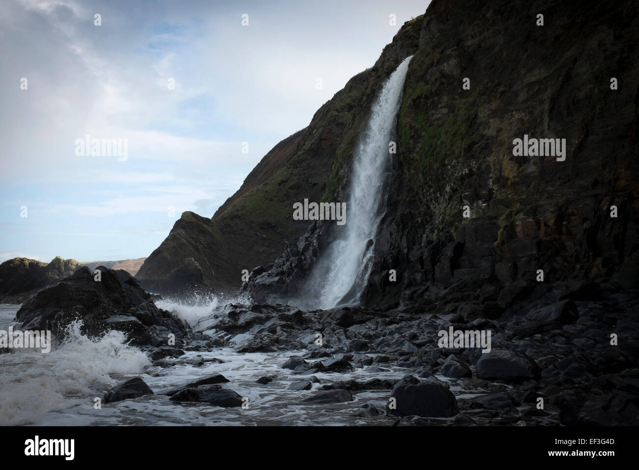 A waterfall cascading over rocks on to the beach in the village of ...