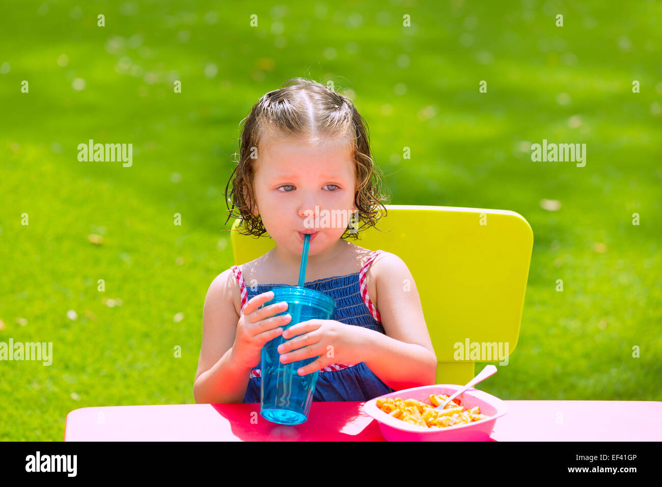 Toddler kid girl drinking eating macaroni pasta in garden turf grass ...