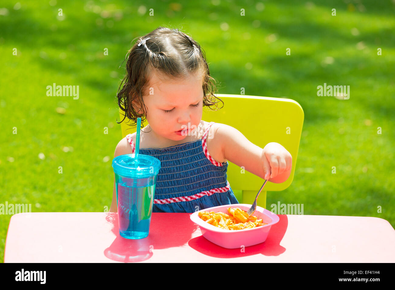 Toddler kid girl eating macaroni tomato pasta in garden turf grass ...