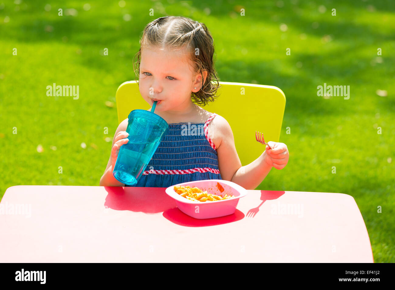Toddler kid girl drinking eating macaroni pasta in garden turf grass ...
