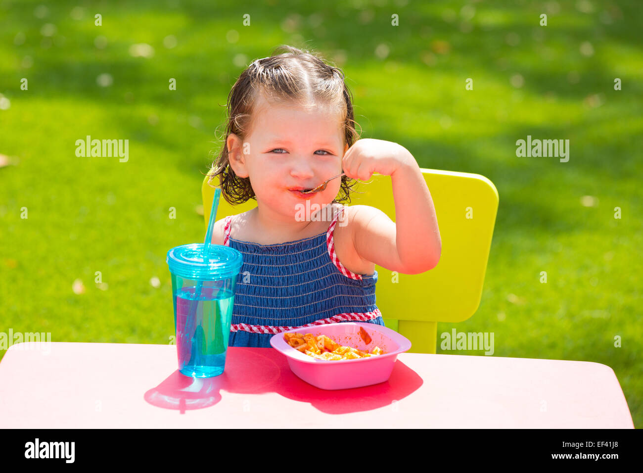 Toddler kid girl eating macaroni tomato pasta in garden turf grass ...
