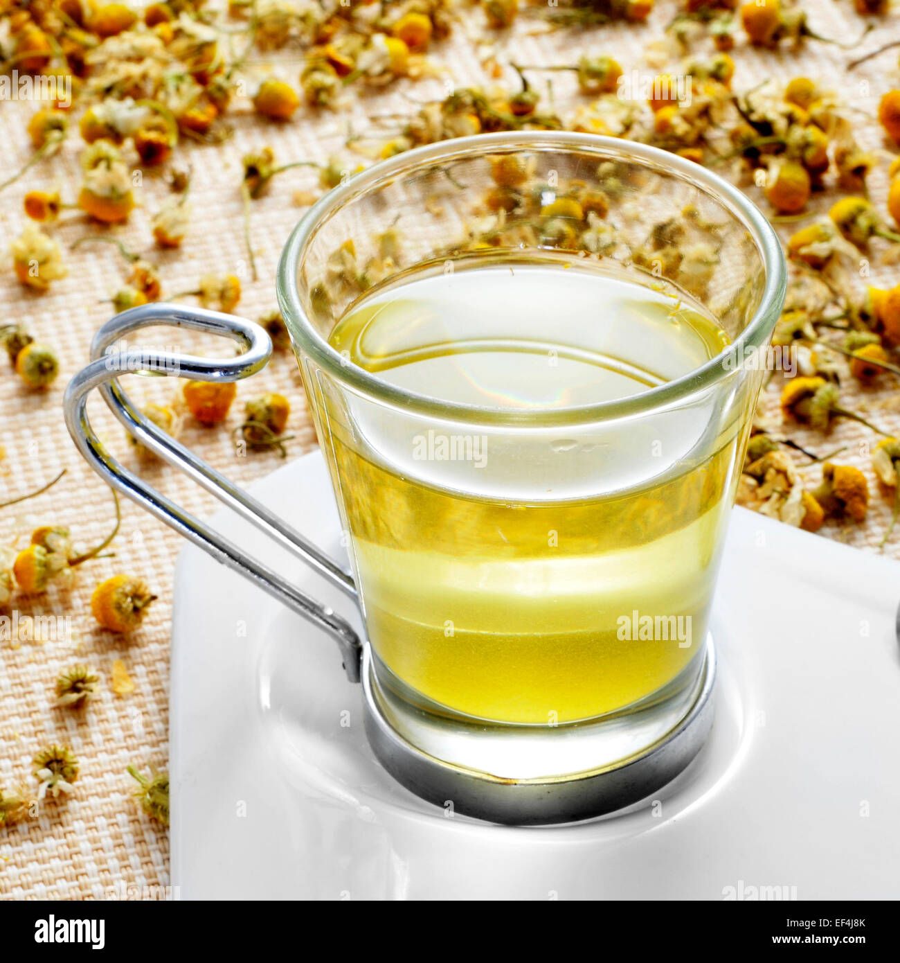 closeup of a glass cup with chamomile tea and a pile of dried chamomile ...