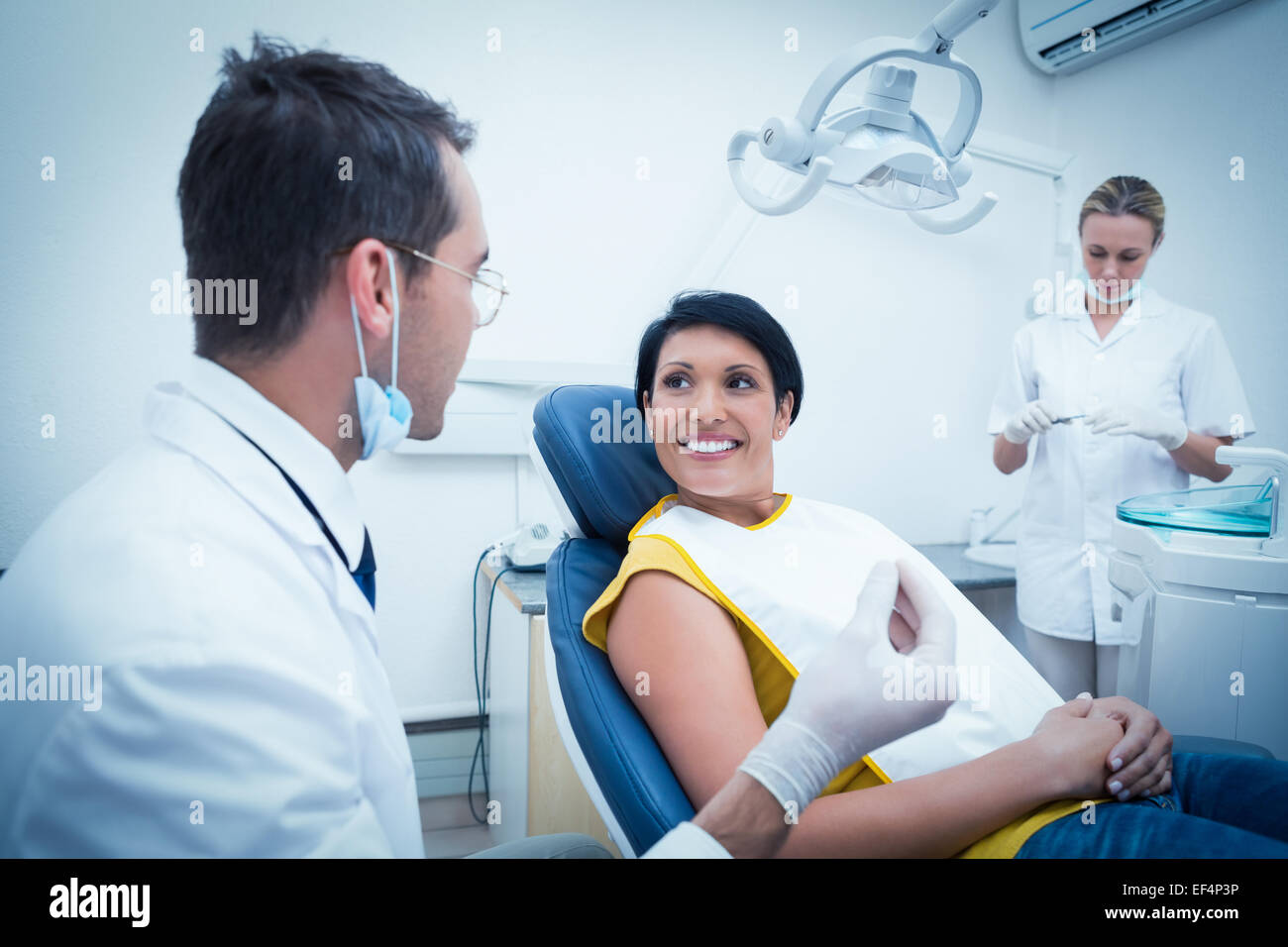 Dentist and assistant with smiling female patient Stock Photo - Alamy