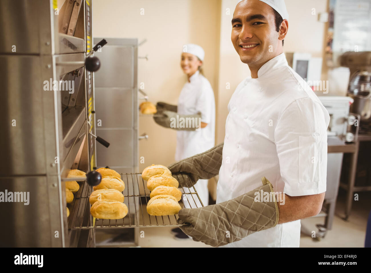 Baker smiling at camera taking rolls out of oven Stock Photo - Alamy