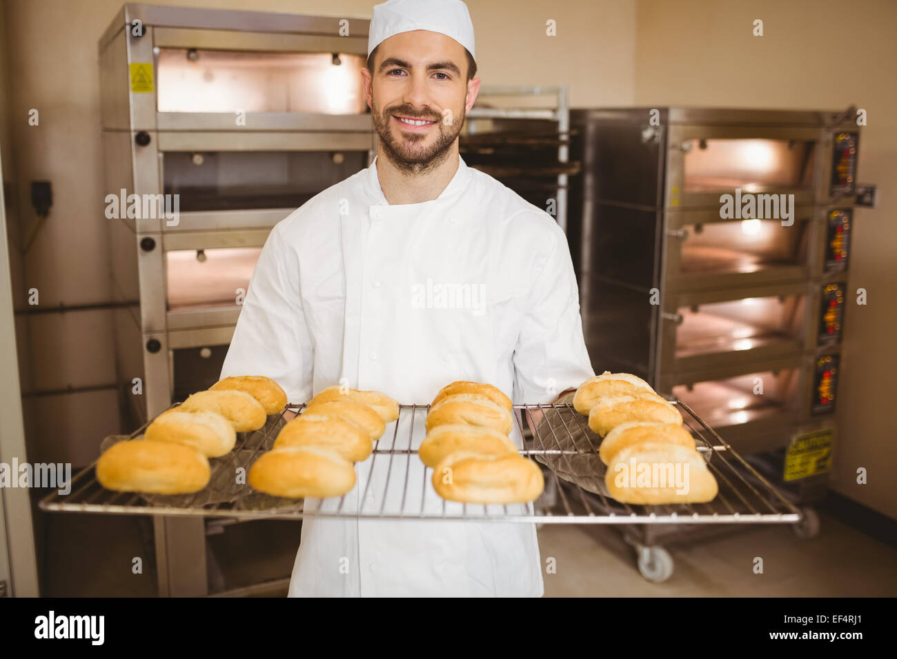 Baker smiling at camera holding rack of rolls Stock Photo - Alamy