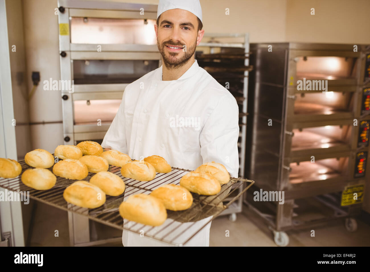 Baker smiling at camera holding rack of rolls Stock Photo - Alamy