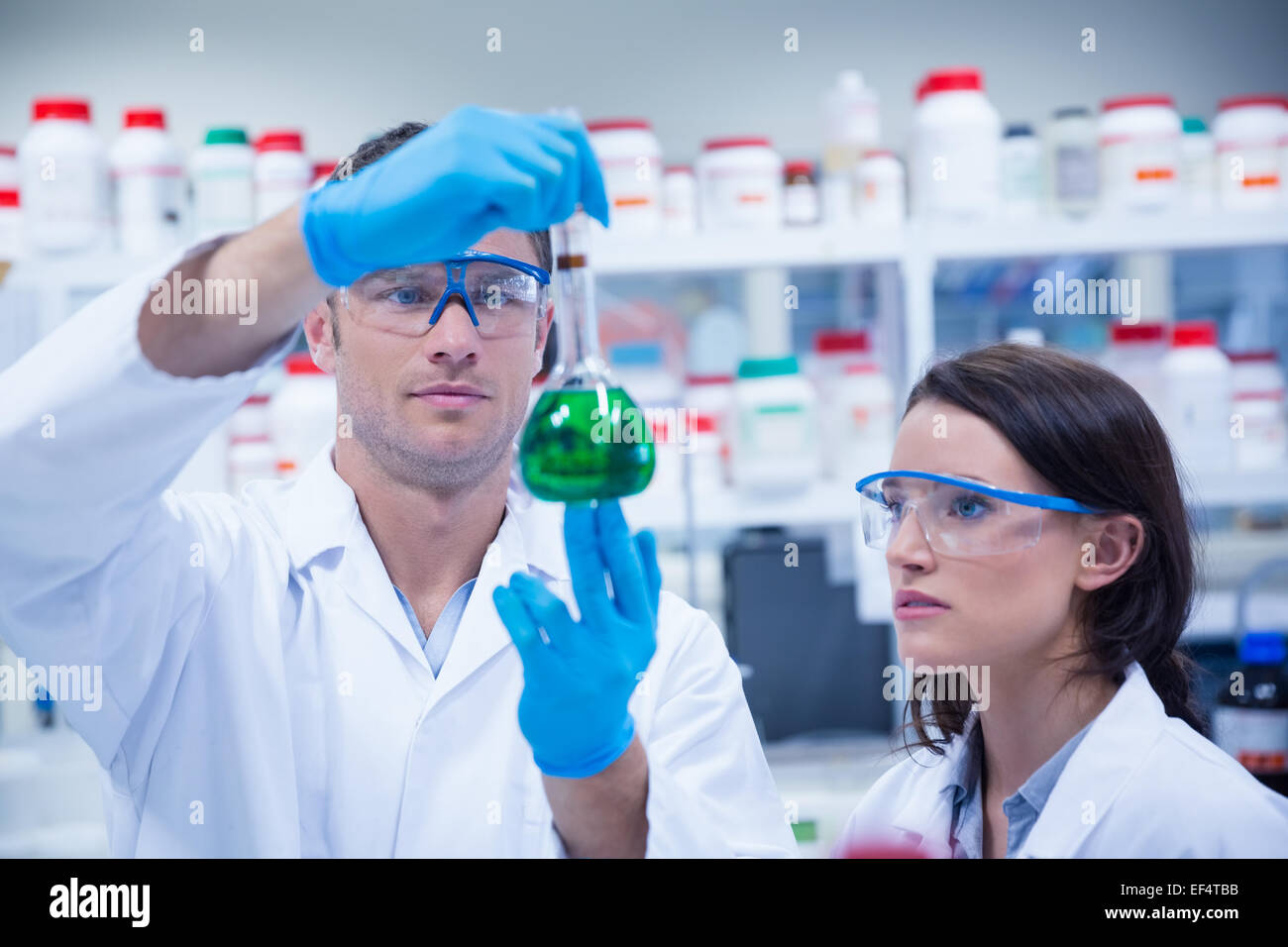 Chemist team looking beaker of green chemical Stock Photo - Alamy
