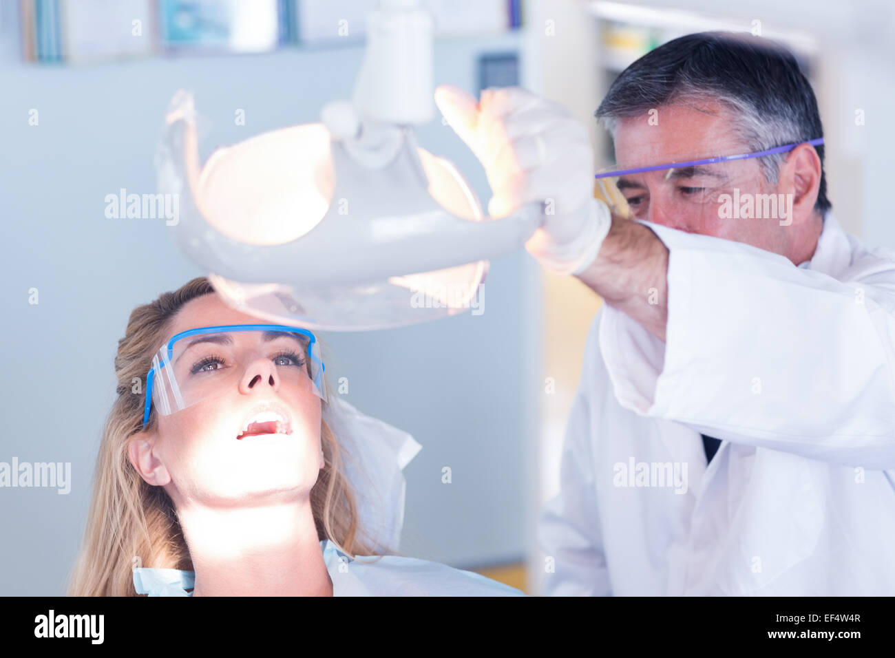Dentist examining a patients teeth in chair under bright light Stock ...