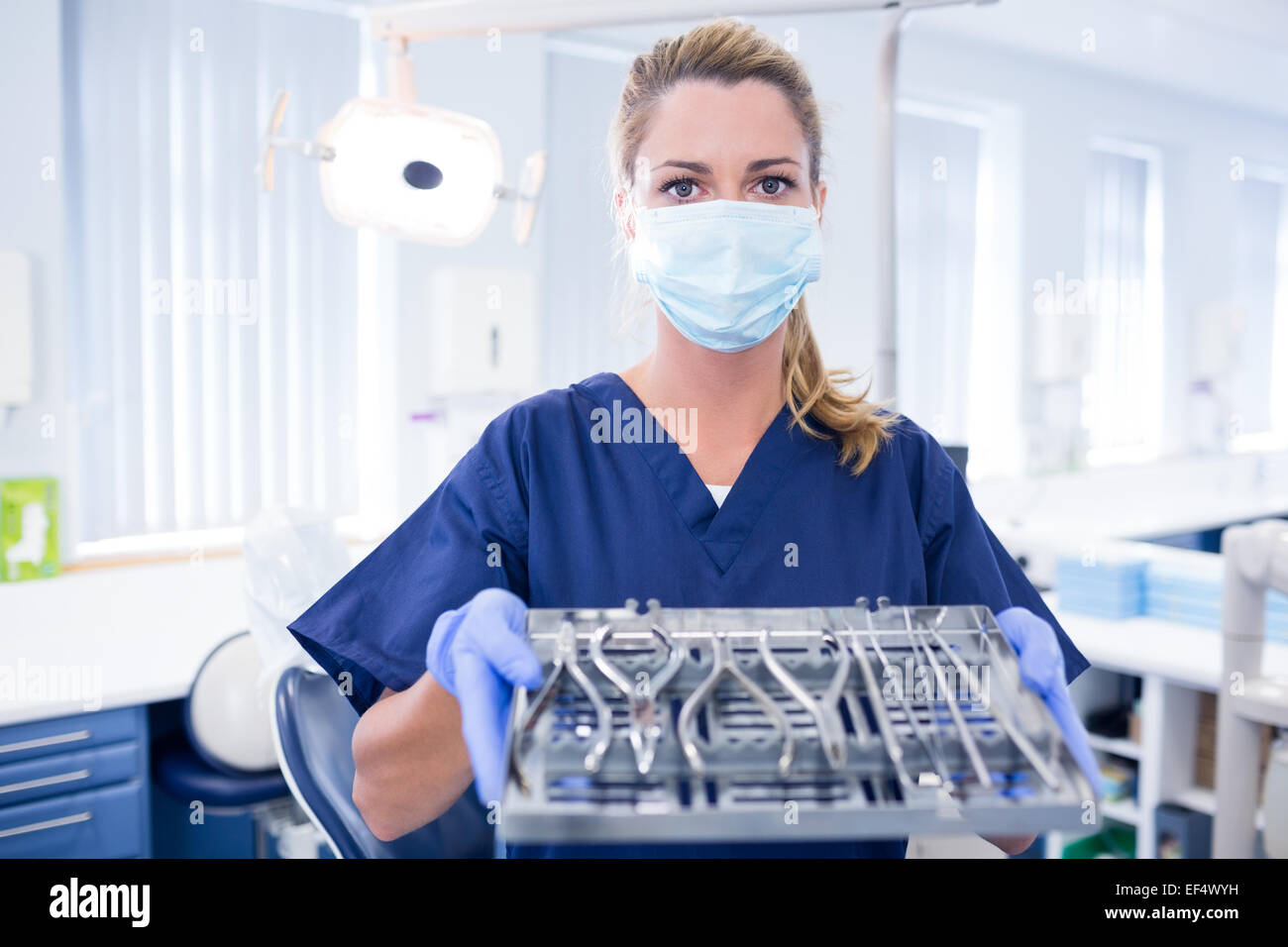 Dentist in blue scrubs holding tray of tools Stock Photo - Alamy