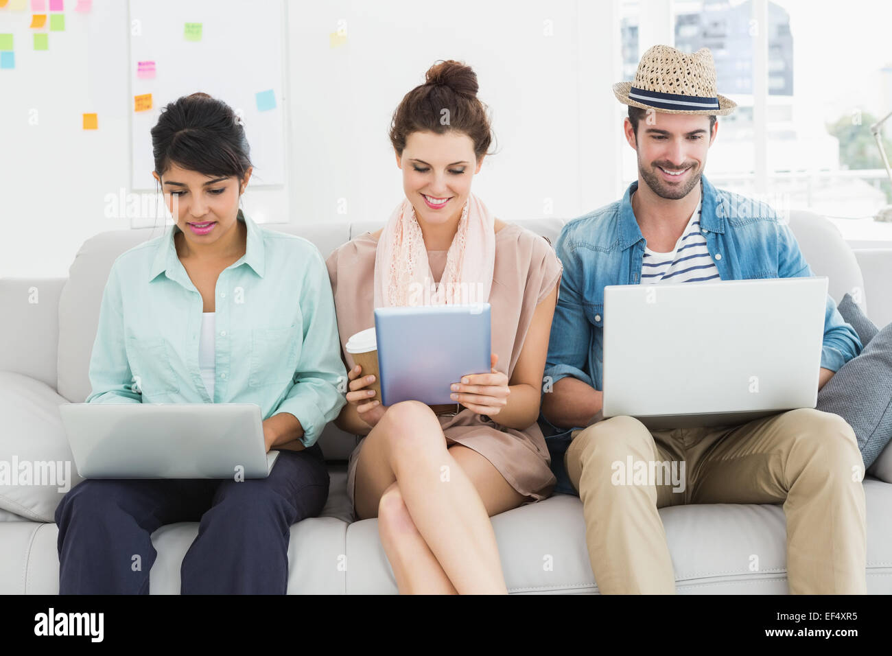 Smiling colleagues on couch using laptop and tablet Stock Photo - Alamy