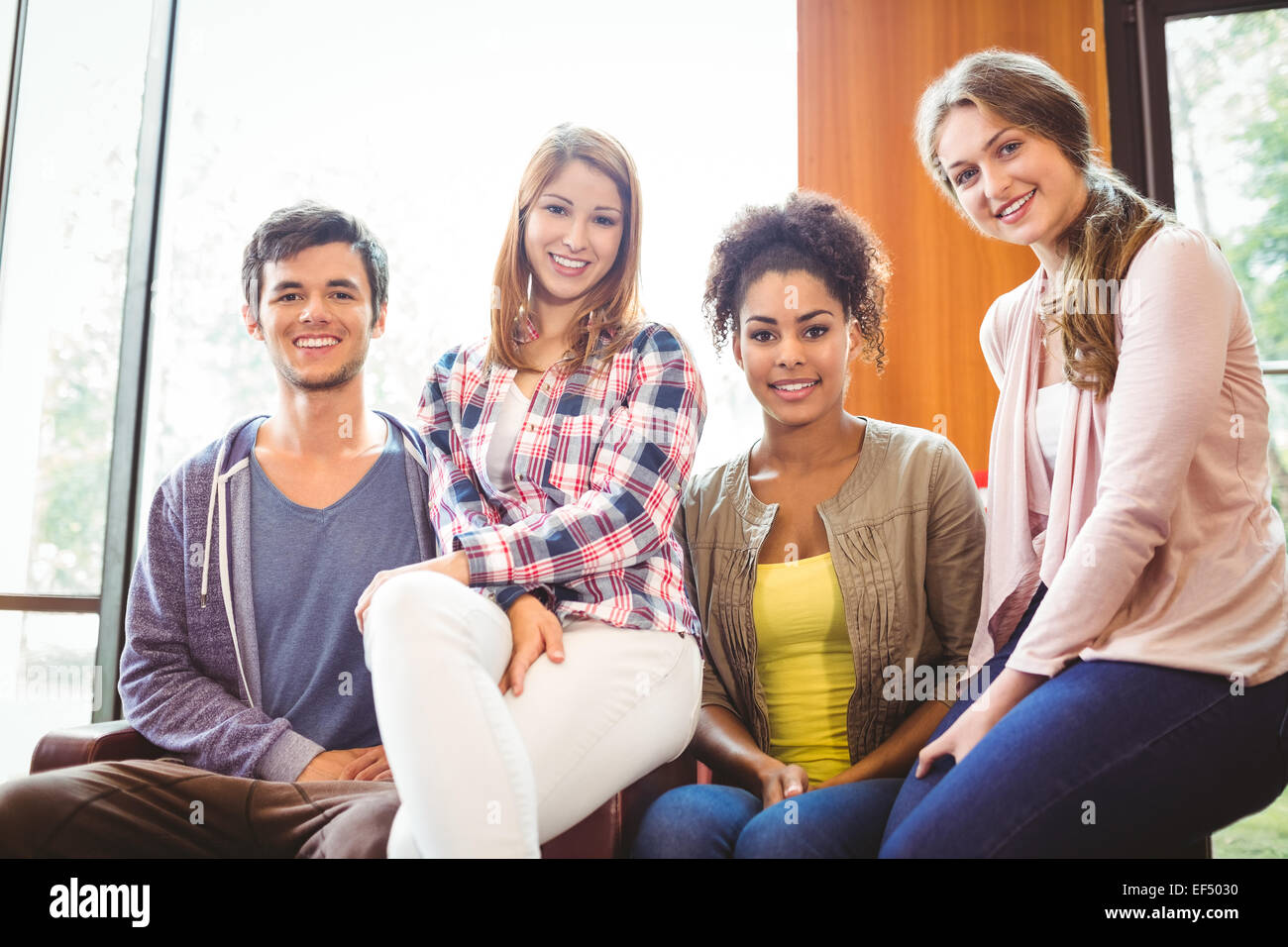 Happy students sitting on couch smiling at camera Stock Photo - Alamy