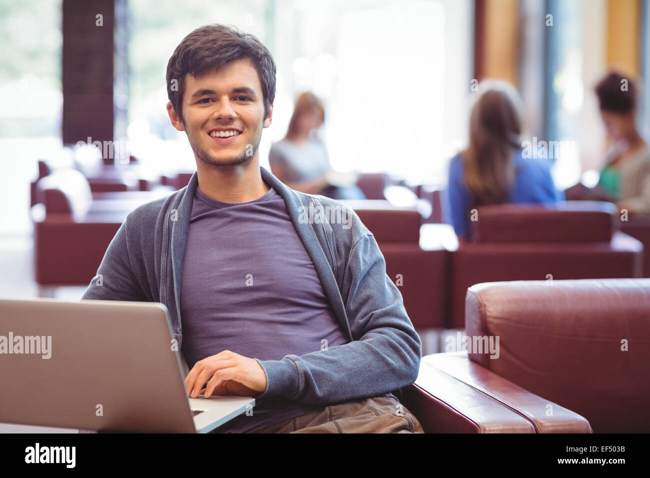 Happy young student sitting on couch using laptop Stock Photo - Alamy