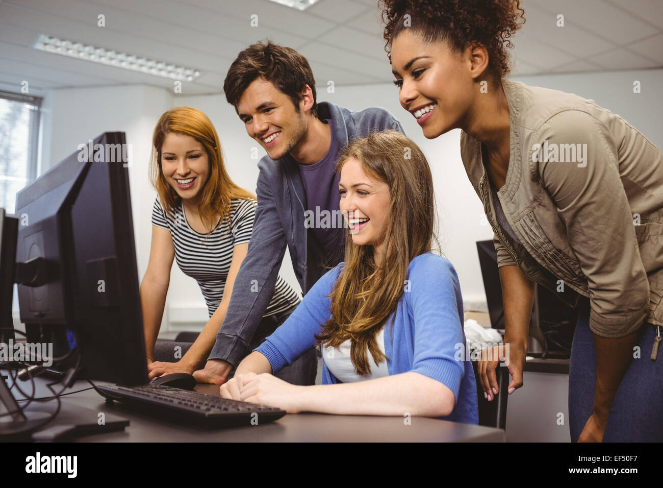 Smiling students sitting at desk using computer together Stock Photo ...