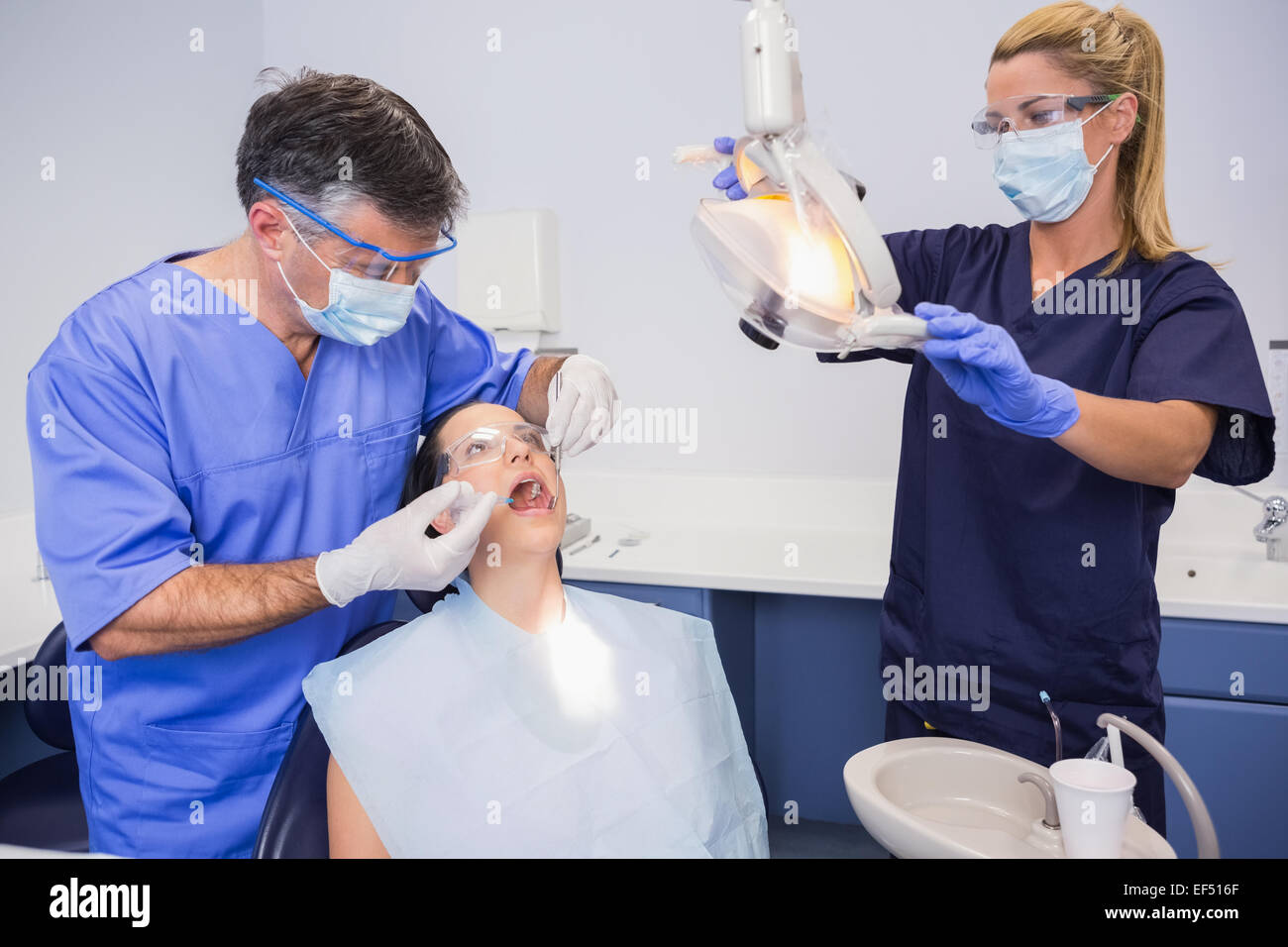Dentist doing injection to his patient and nurse adjusting the light ...