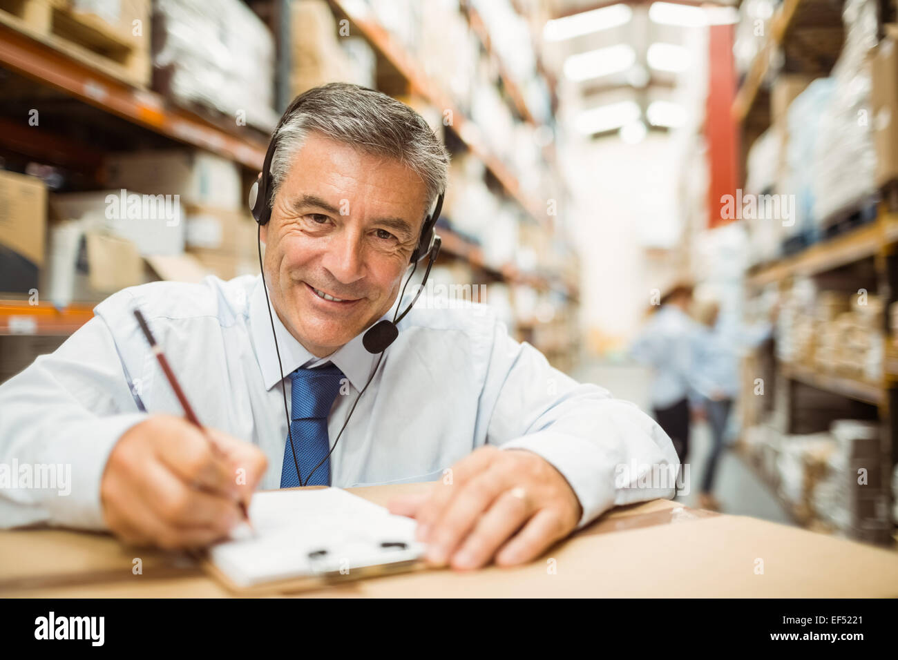 Smiling warehouse manager writing on clipboard Stock Photo - Alamy