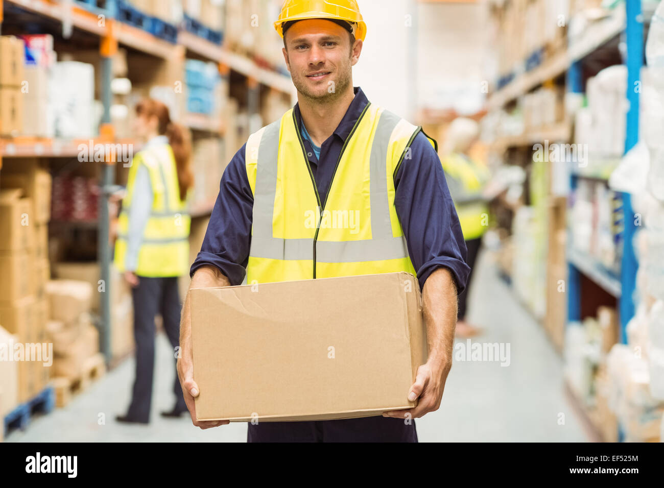 Warehouse worker smiling at camera carrying a box Stock Photo - Alamy