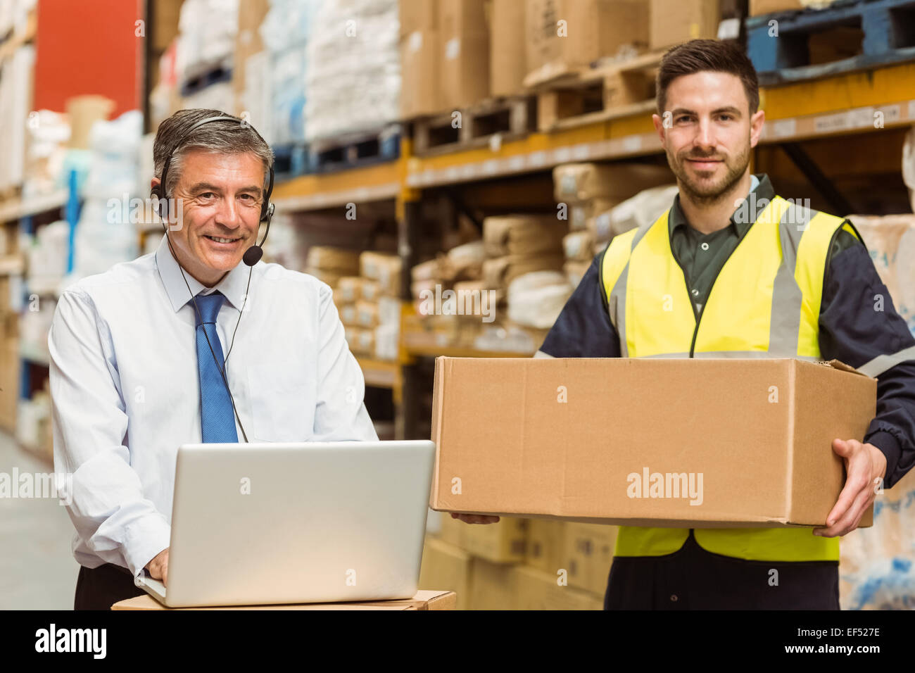 Smiling warehouse manager using laptop Stock Photo - Alamy