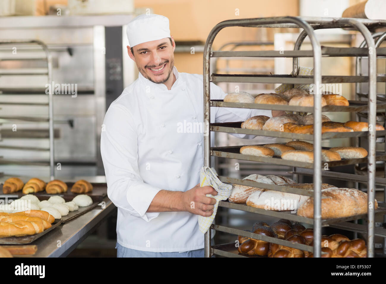 Smiling baker pushing tray of bread Stock Photo - Alamy