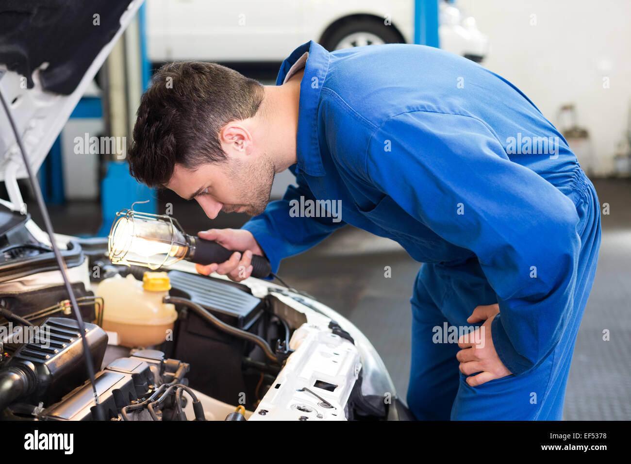 Mechanic examining under hood of car with torch Stock Photo - Alamy