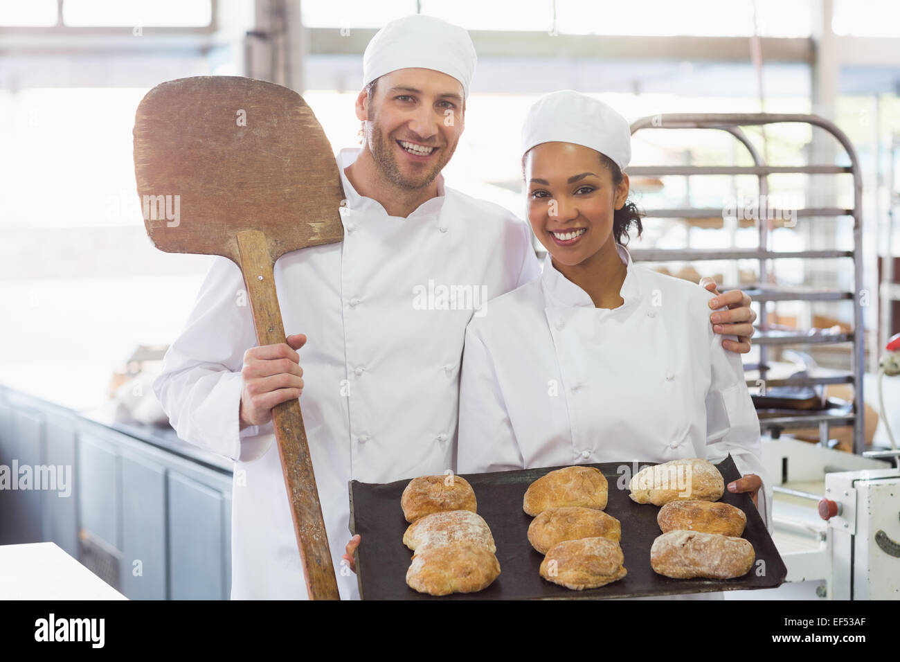 Team of bakers smiling at camera with trays of loaves Stock Photo - Alamy